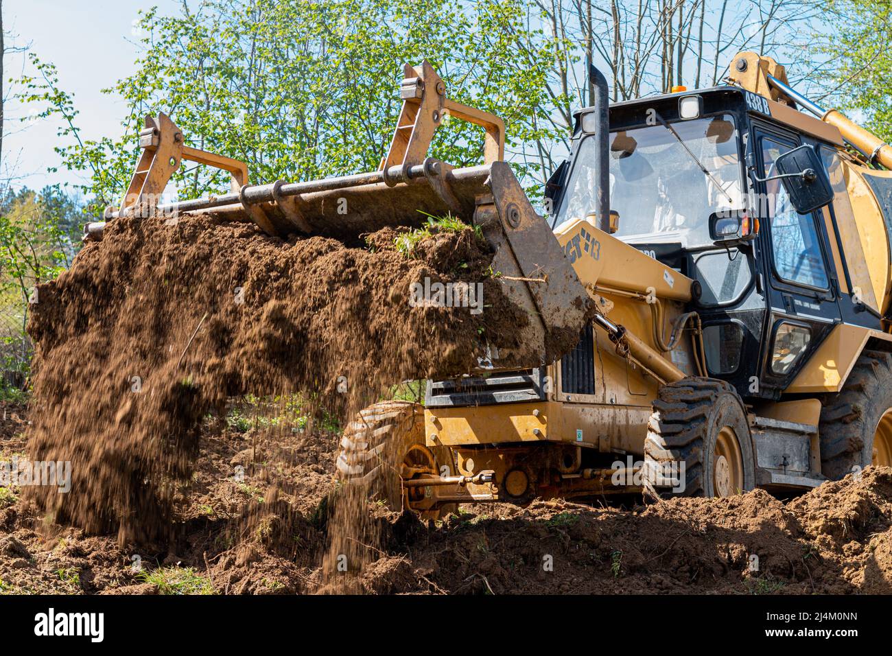 Clearing and leveling a private land plot. Yellow excavator driving ...