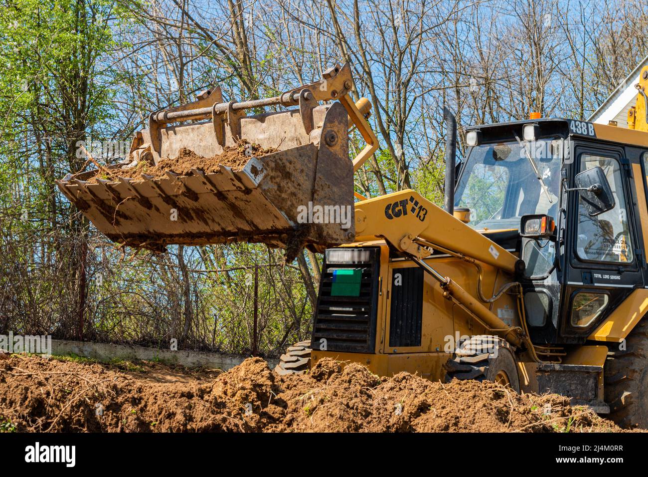 Clearing and leveling a private land plot. Yellow excavator driving ...