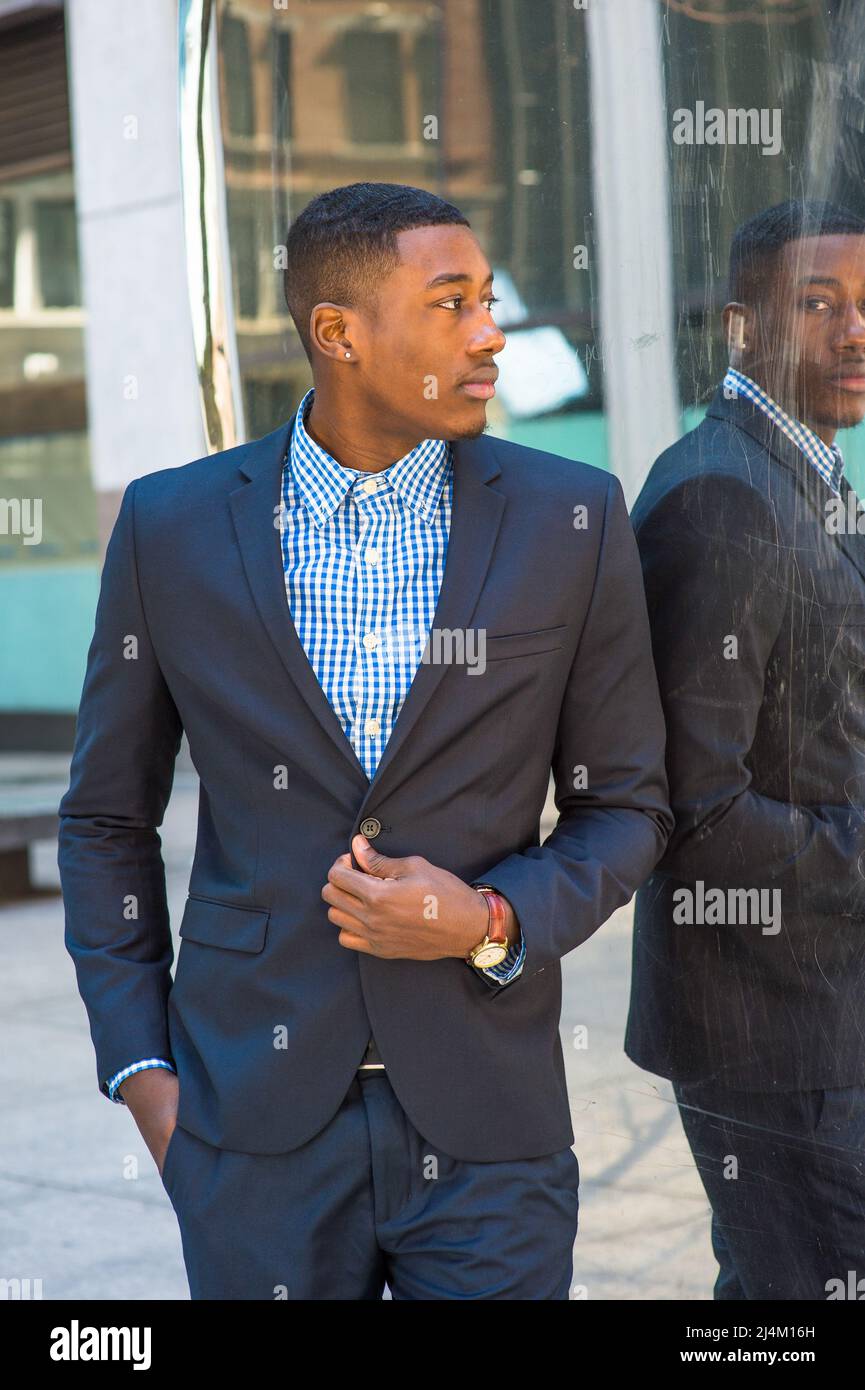 A young black businessman is standing by a mirror and looking at the ...