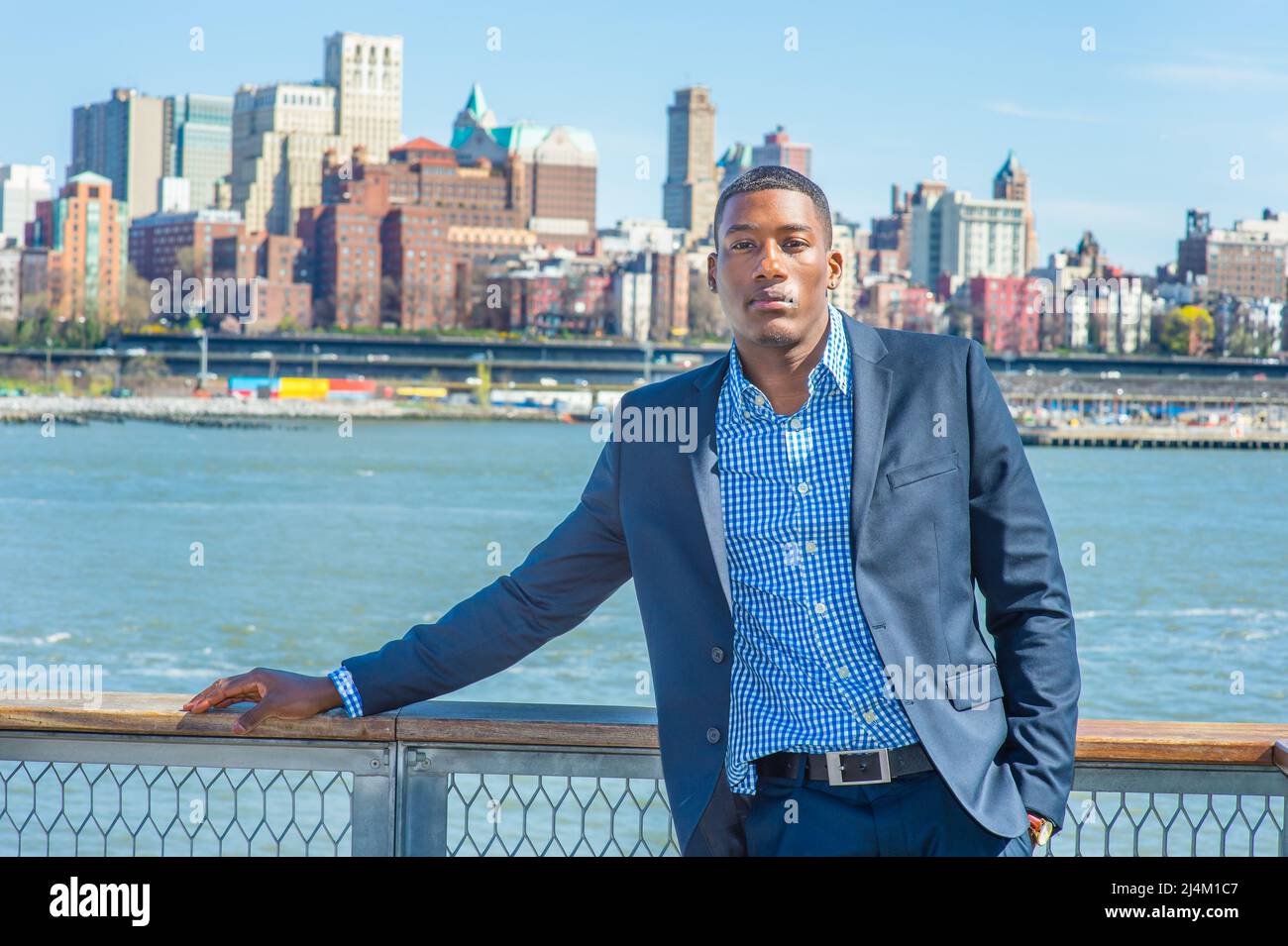 A young black businessman is standing by the river, looking forward ...