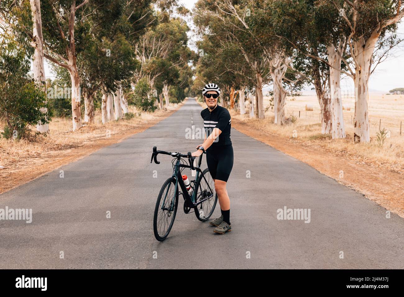 Woman cyclist taking rest standing of the center of the empty road ...