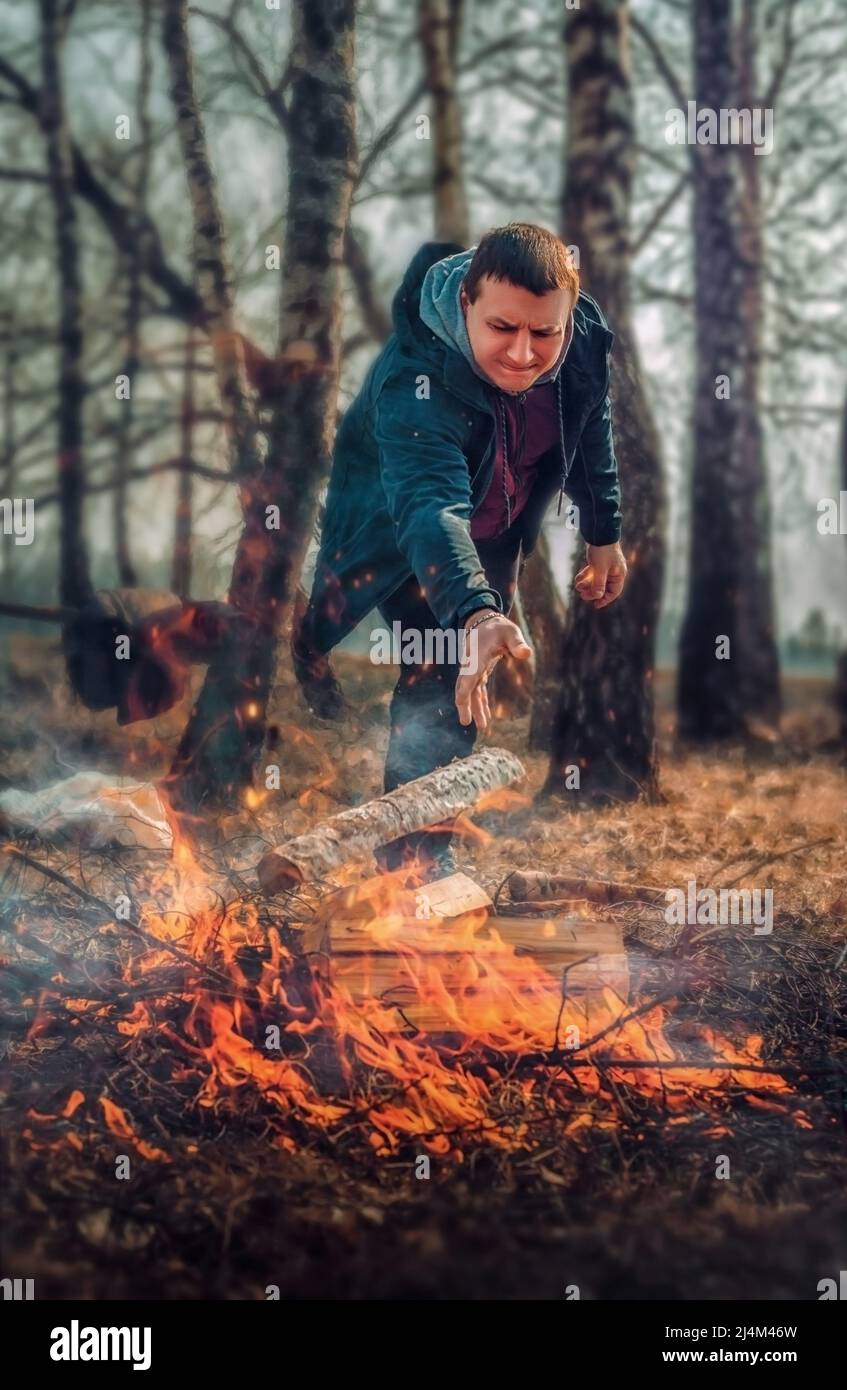 a man kindles a fire in the forest and throws firewood into the fire ...