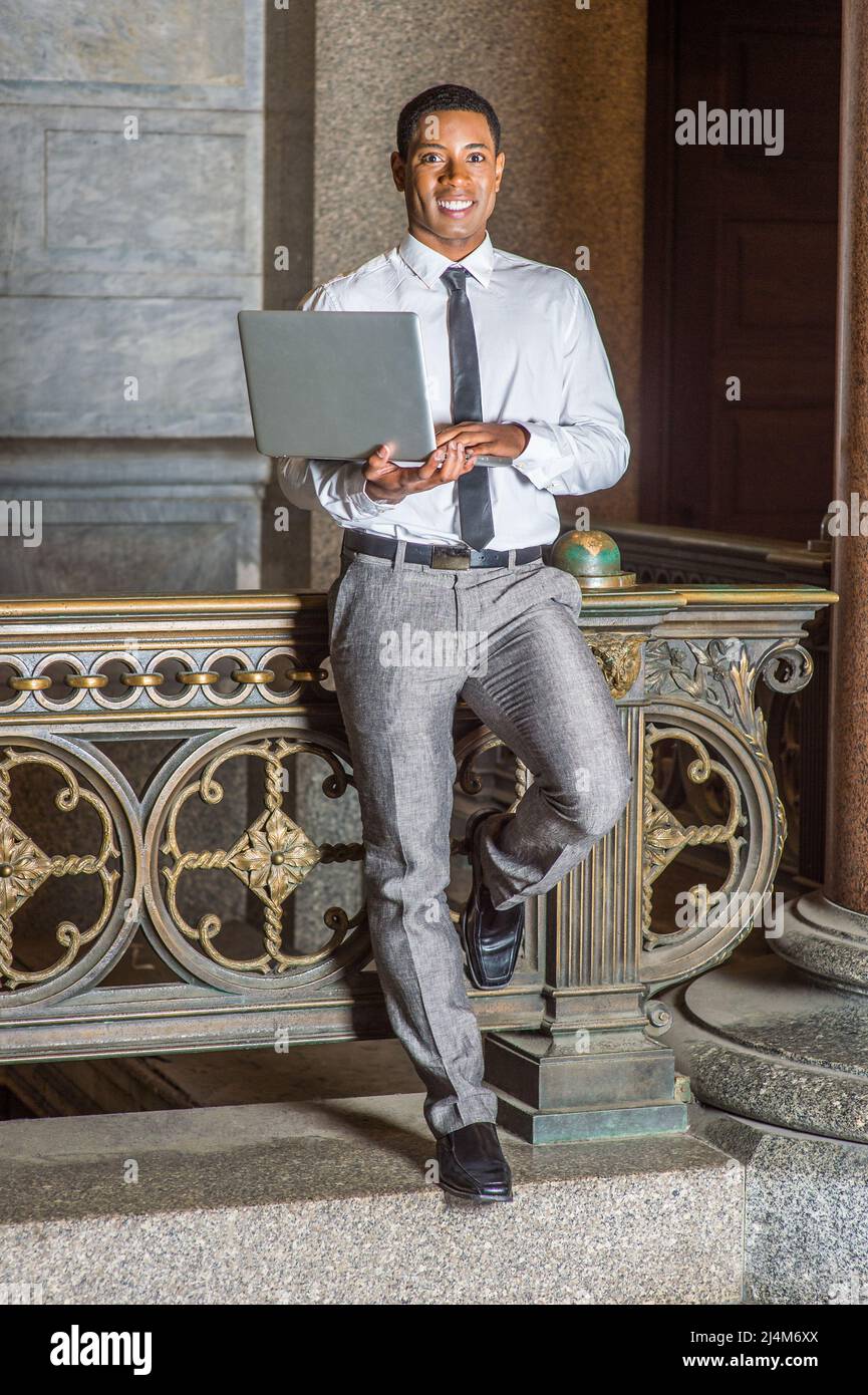 Wearing a white shirt, a black tie, gray pants, holding a laptop ...