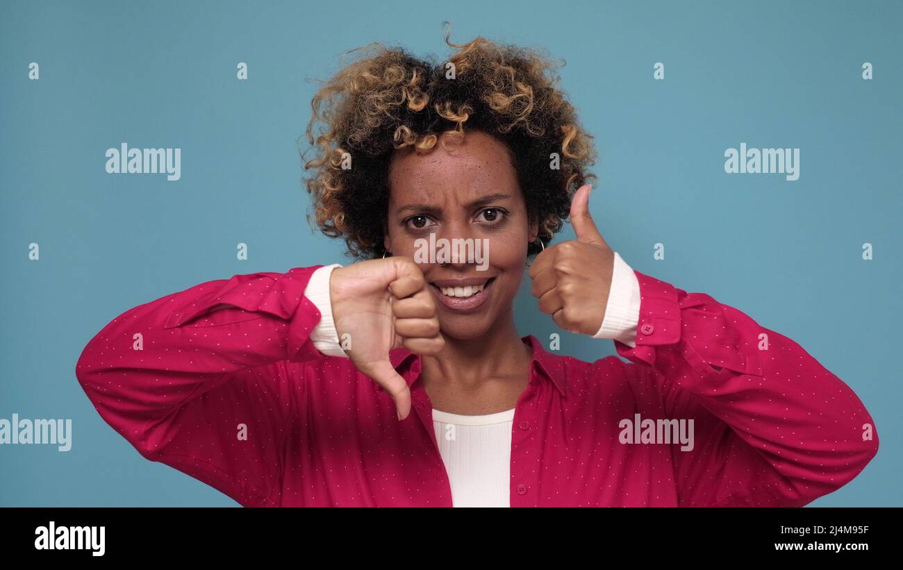 Beautiful african woman being confused making thumbs up and down ...