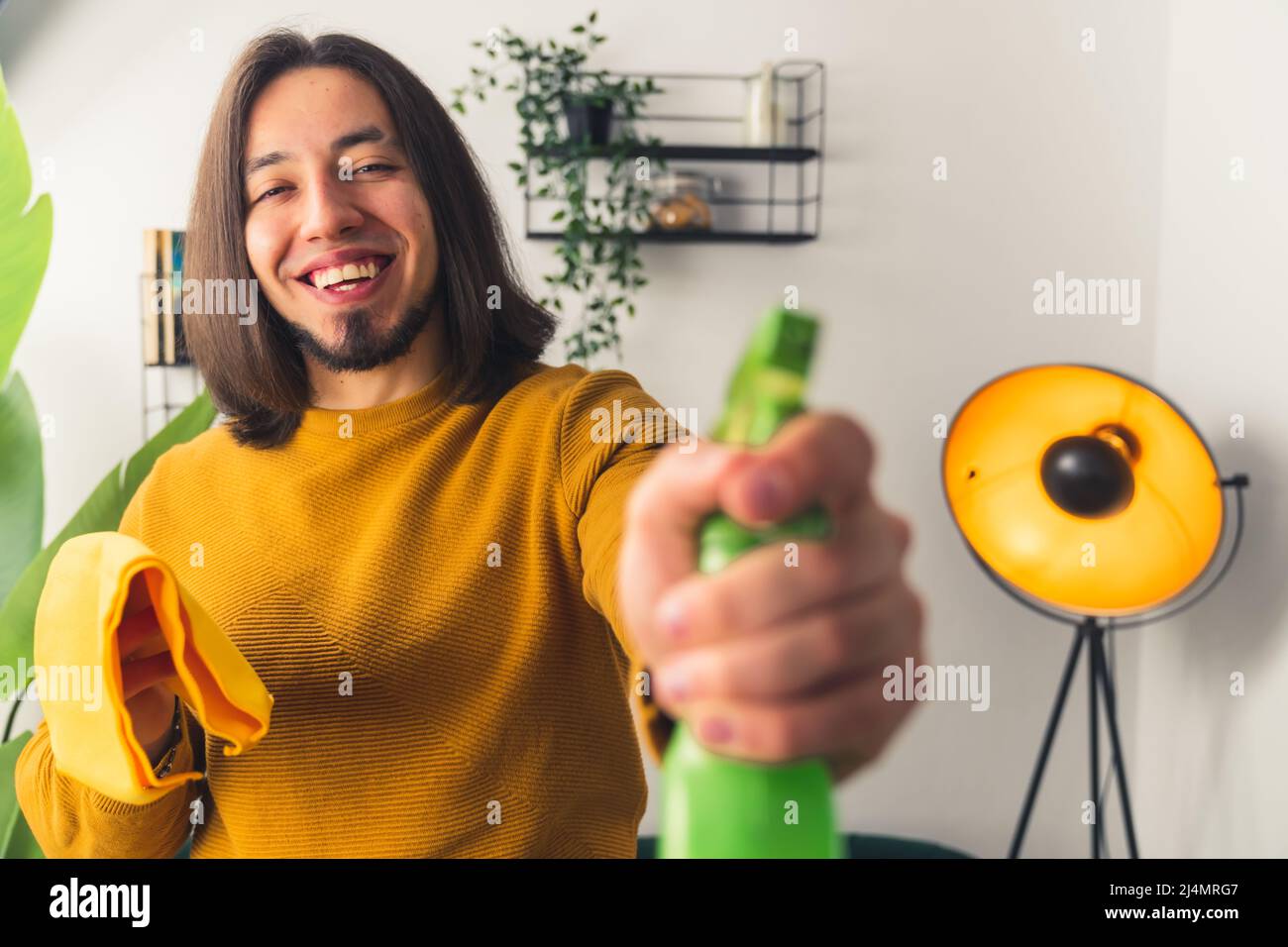 Young smiling man holds sprayer and cloth copy space medium shot home ...
