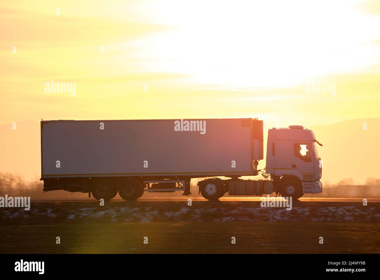 Semi-truck with cargo trailer driving on highway hauling goods in evening. Delivery ...
