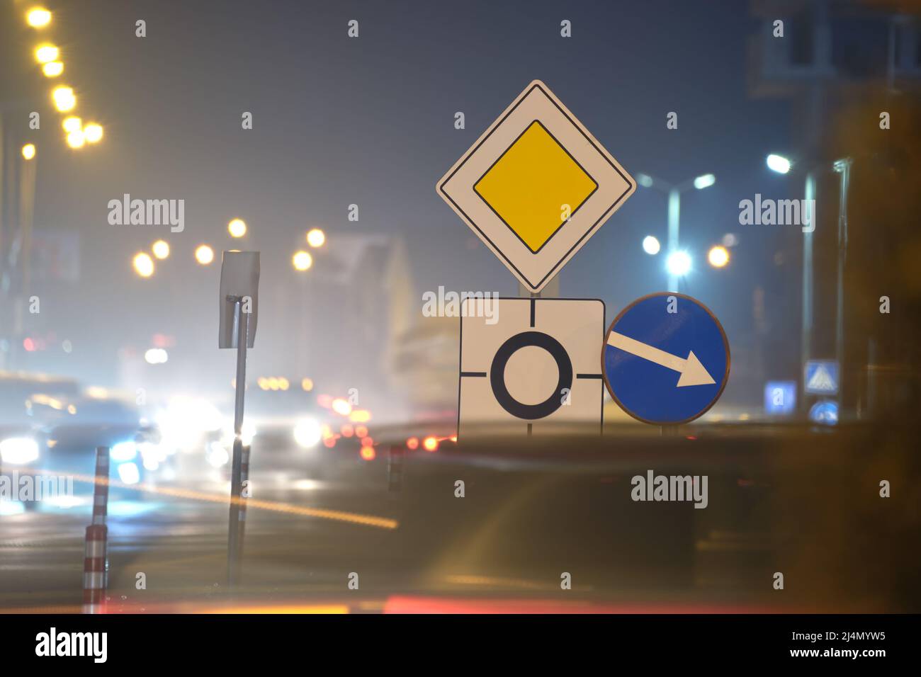 Roundabout road signs with blurred cars on city street traffic at night ...