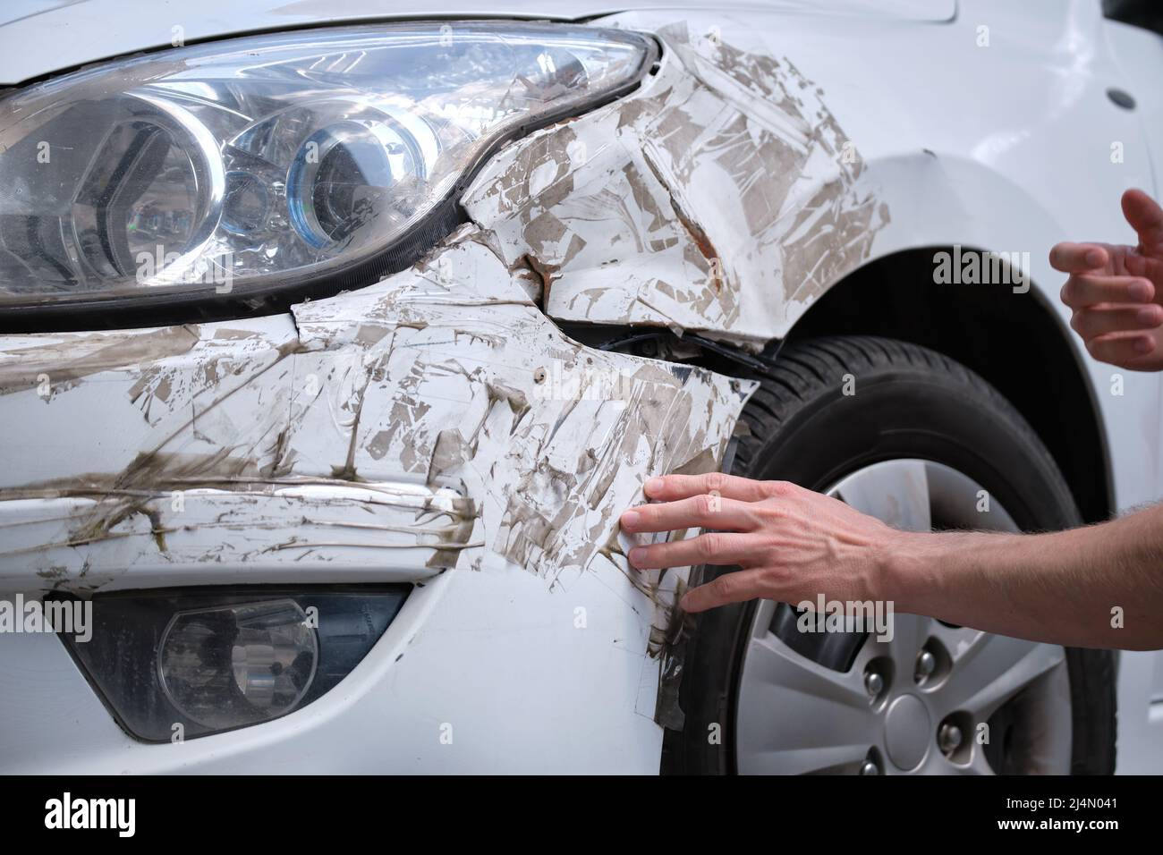 Driver hand examining dented car with damaged fender parked on city ...