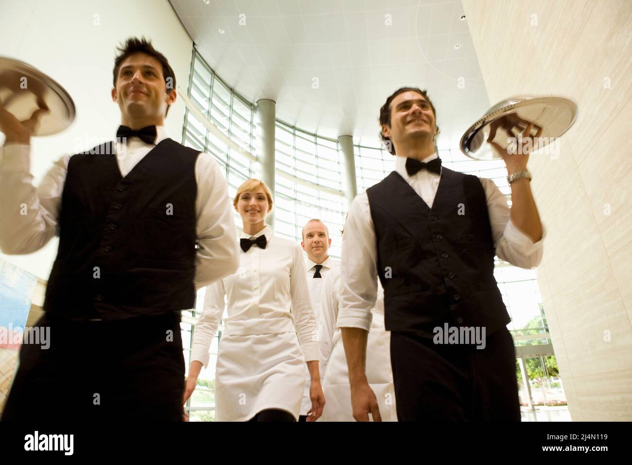 Waiters and waitresses, carrrying trays and covered platters, moving ...