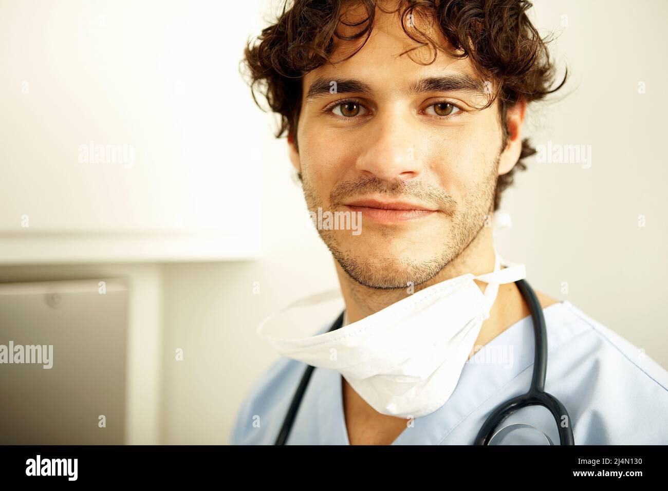 Male healthcare professional in scrubs with surgical mask pulled down ...
