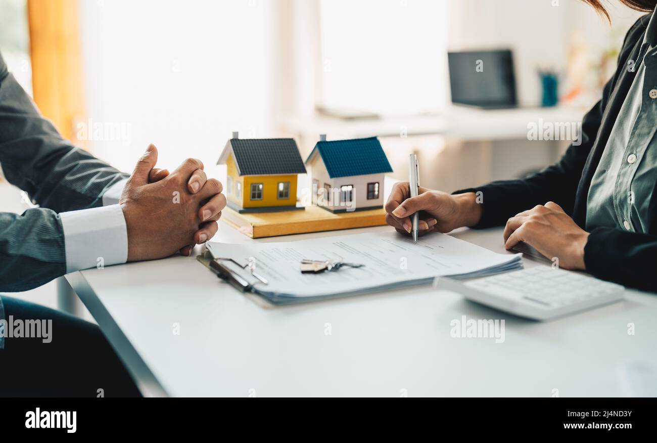 Real estate agent assisting client to sign contract at desk with house ...