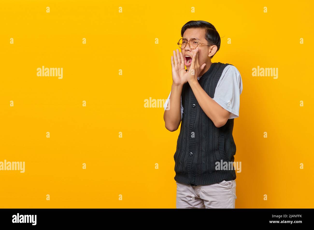 Portrait of screaming young Asian man with shocked expression on yellow ...