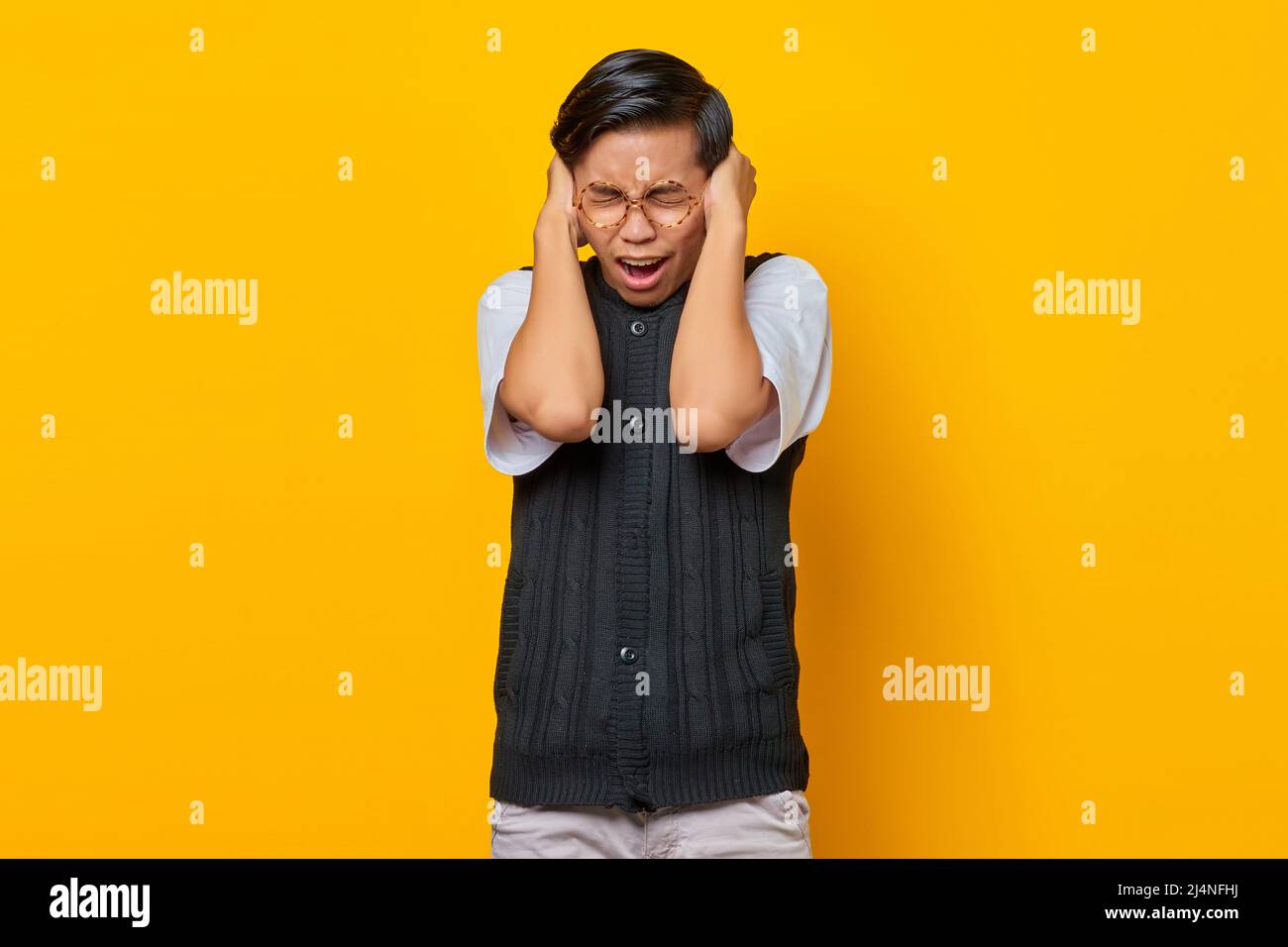 Frustrated Asian young man covering ears with hands isolated over ...