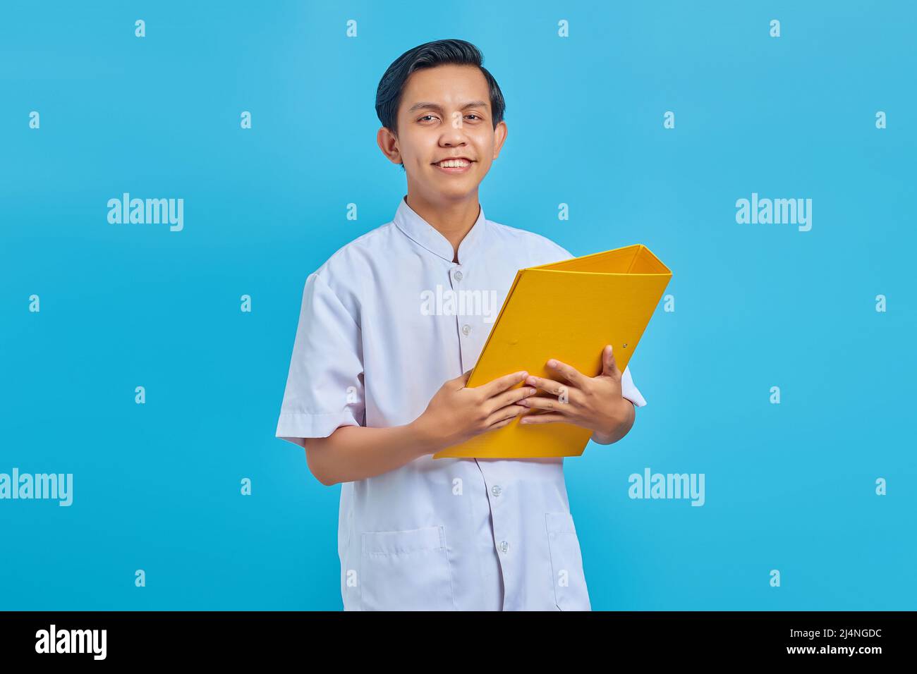 Portrait of cheerful male nurse holding yellow folder on blue ...