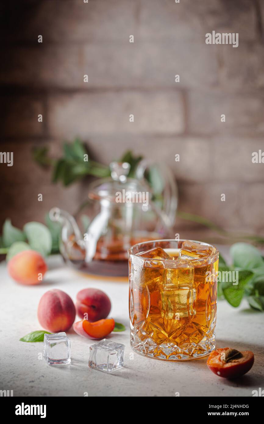 Glass of peach or apricot iced tea with fruit slices against white ...