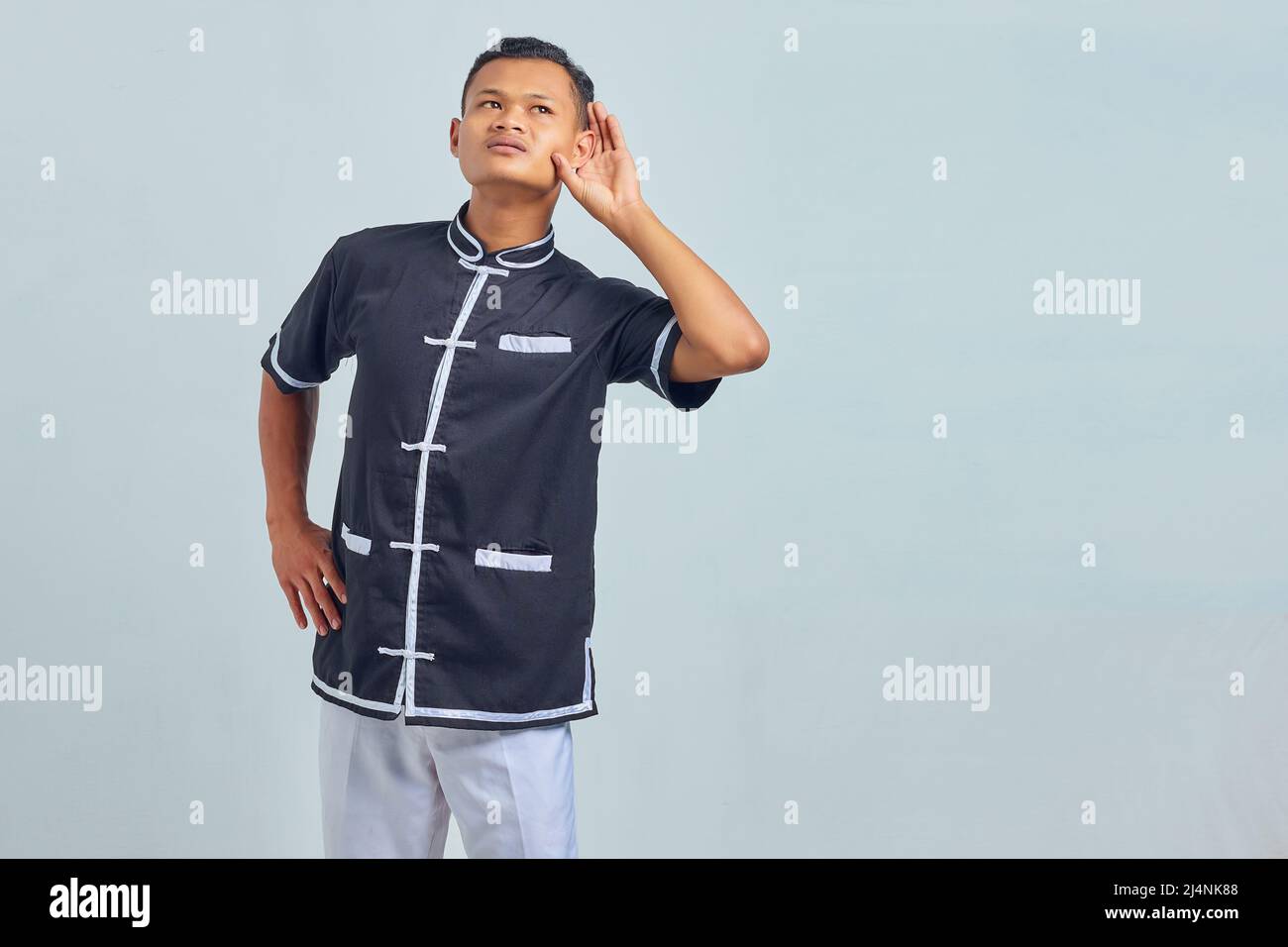 Portrait of cheerful asian young man wearing karate uniform trying to ...