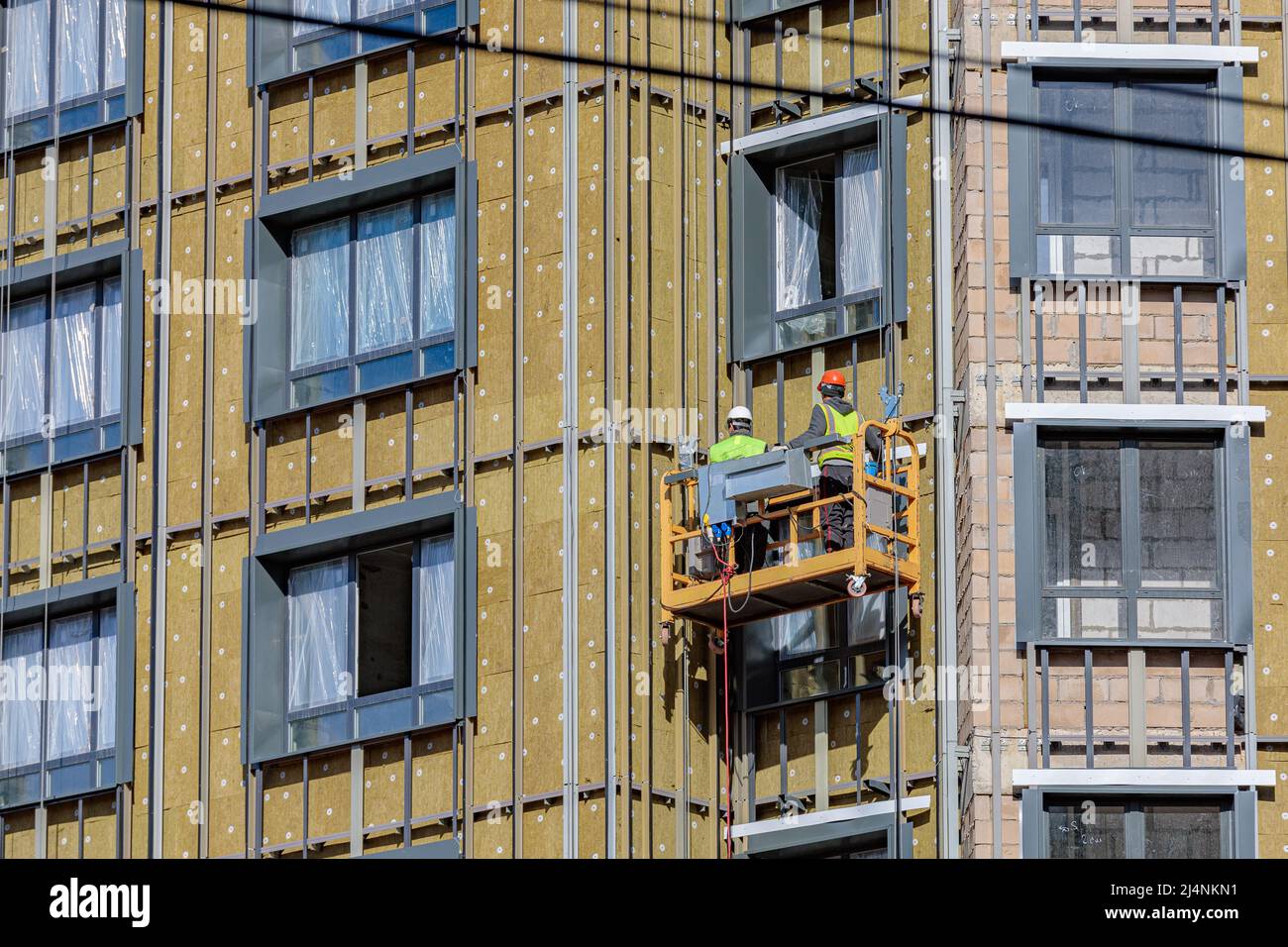 Male builders work on the facade of the building in a suspended cradle ...
