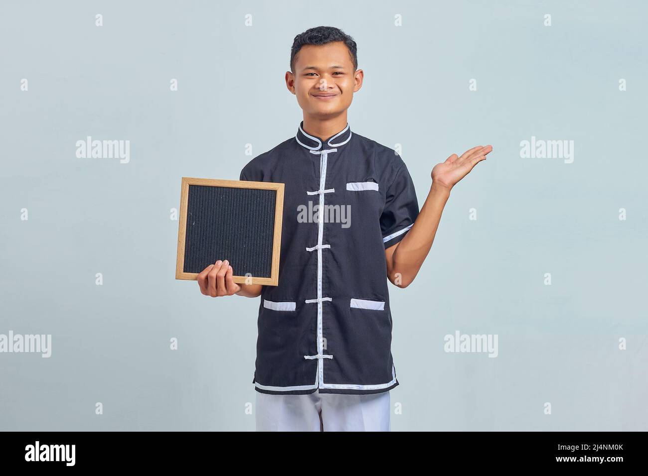 Portrait of cheerful Asian young man wearing karate uniform pointing to ...