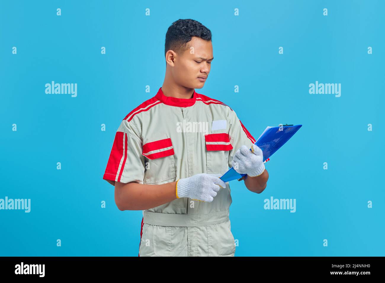 Shocked young Asian mechanic looking at notes on clipboard over blue ...