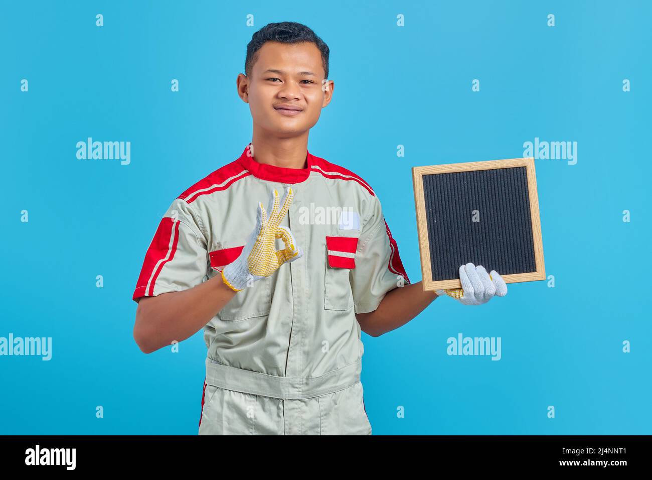 Portrait of cheerful young Asian mechanic holding blank board and doing ...