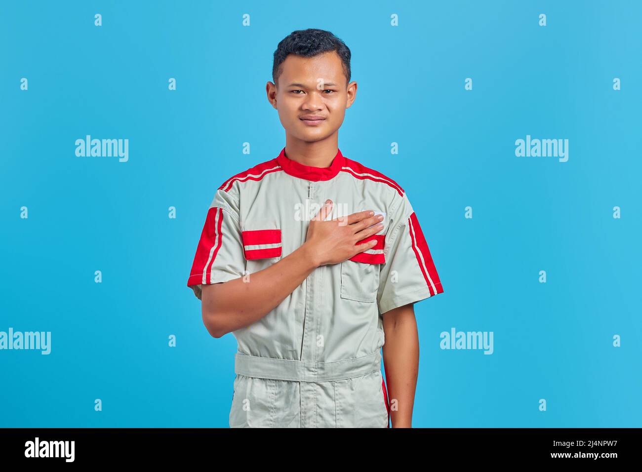 Portrait of smiling young Asian mechanic with palms on chest over blue ...