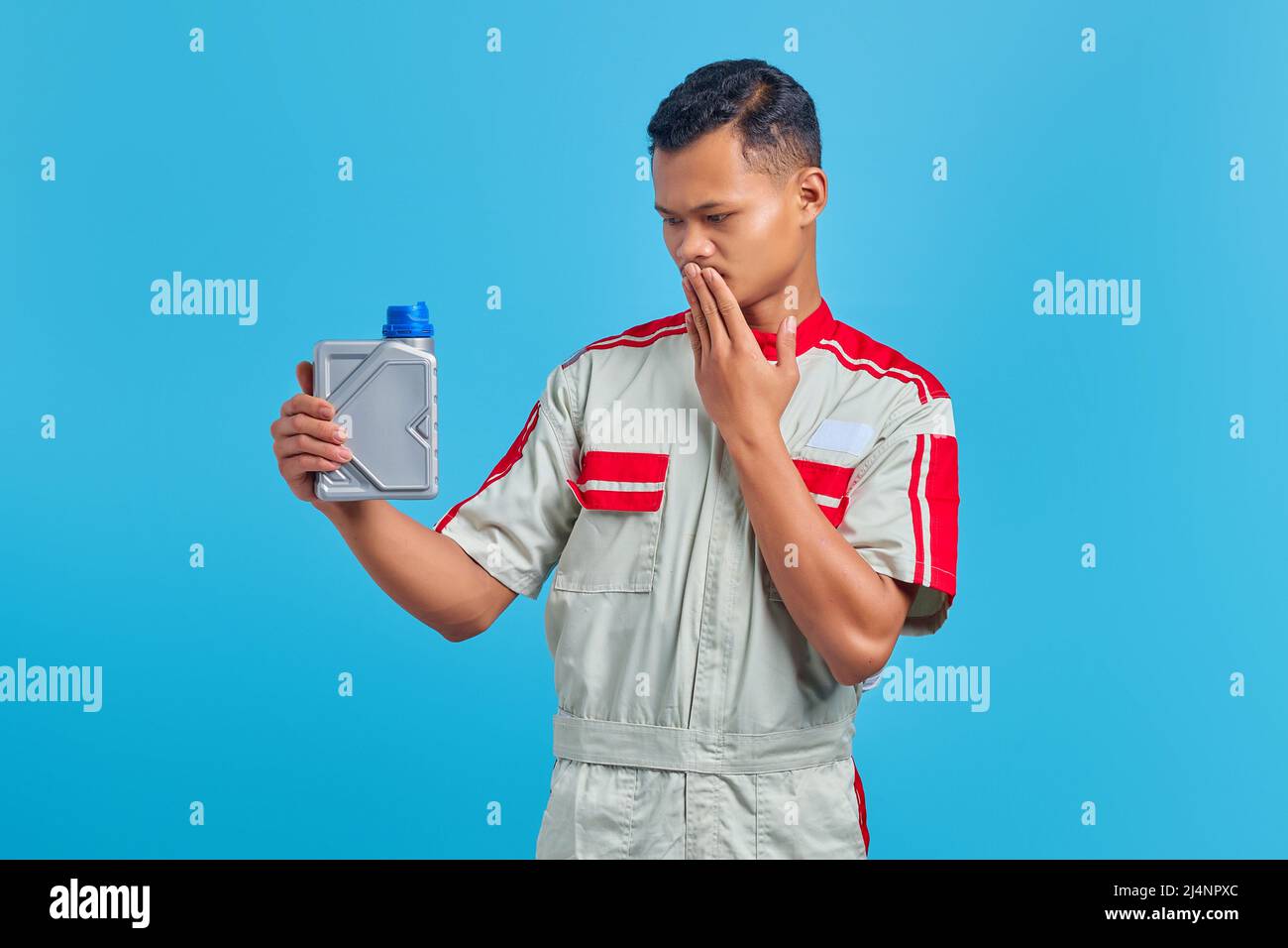 Shocked young Asian mechanic portrait holding engine oil plastic bottle ...