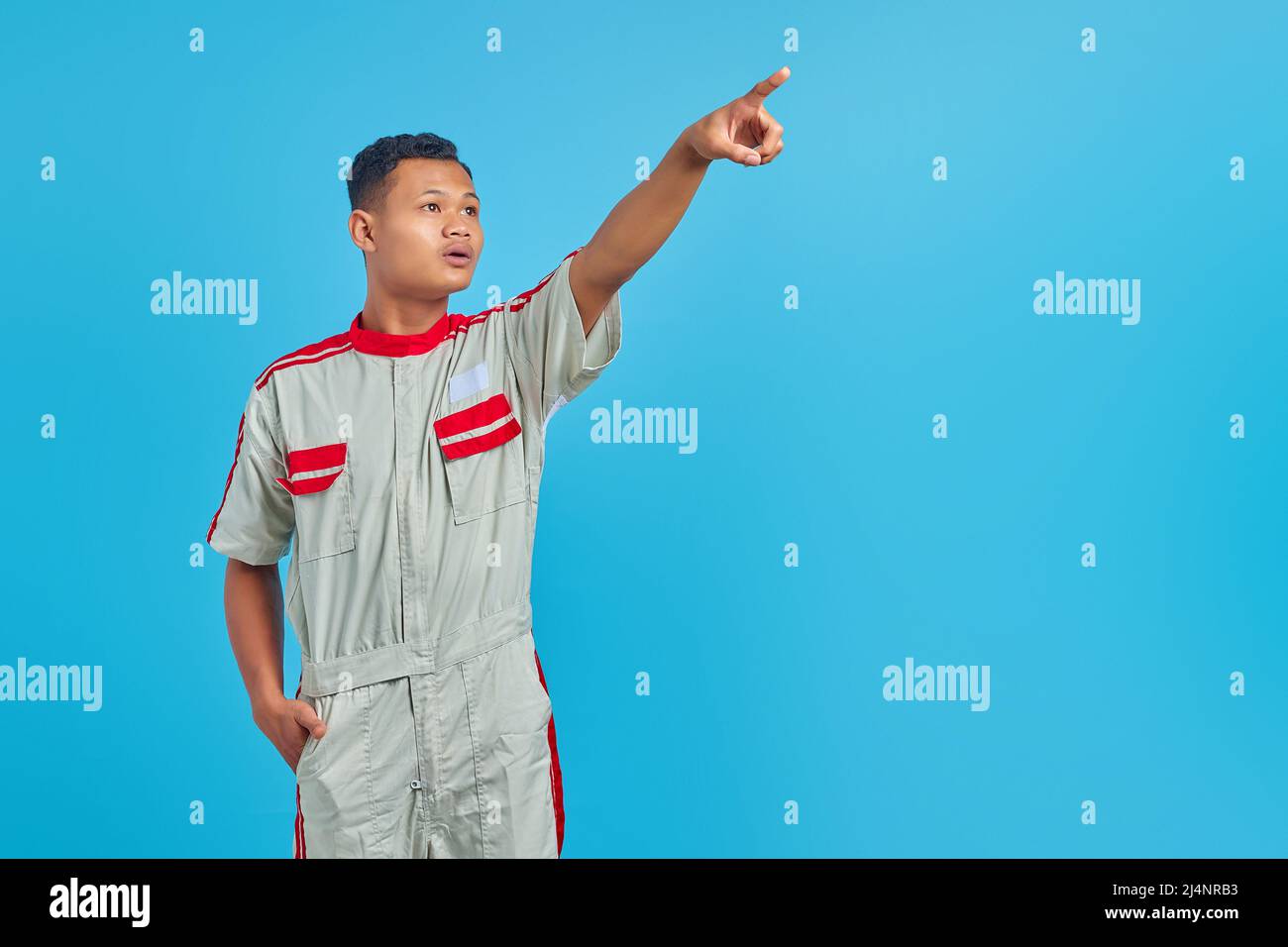 Portrait of angry young Asian mechanic pointing at empty space with ...