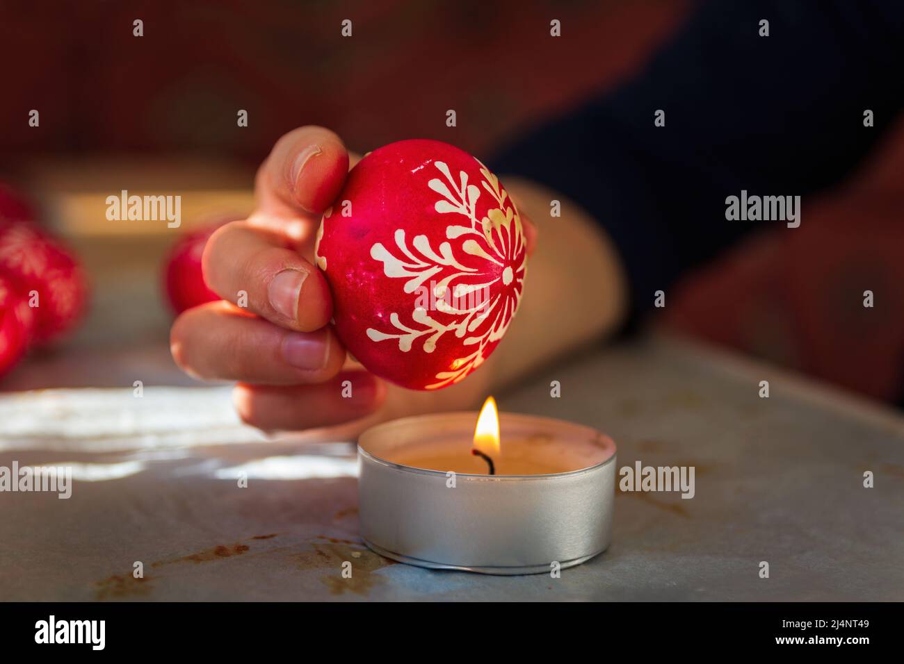 Close up photo of woman hand remove wax from easter egg with candle ...