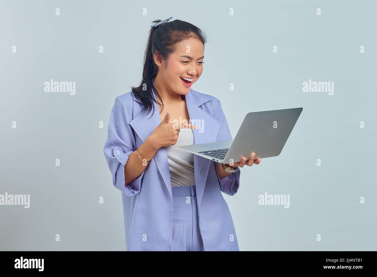 Portrait of cheerful young Asian woman pointing fingers at a laptop isolated on white background ...