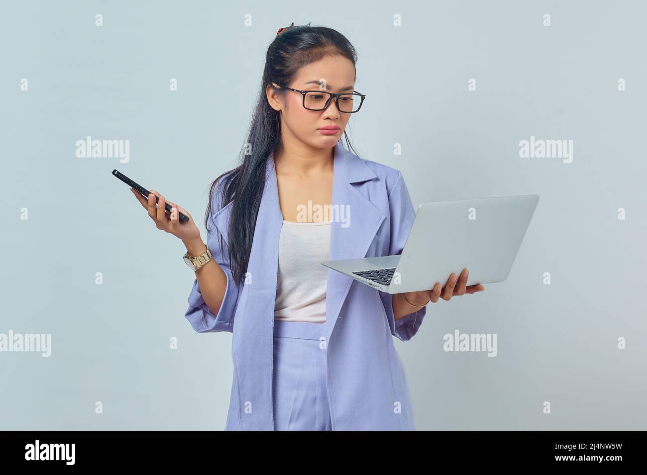 Portrait of young Asian woman standing using laptop and holding mobile ...