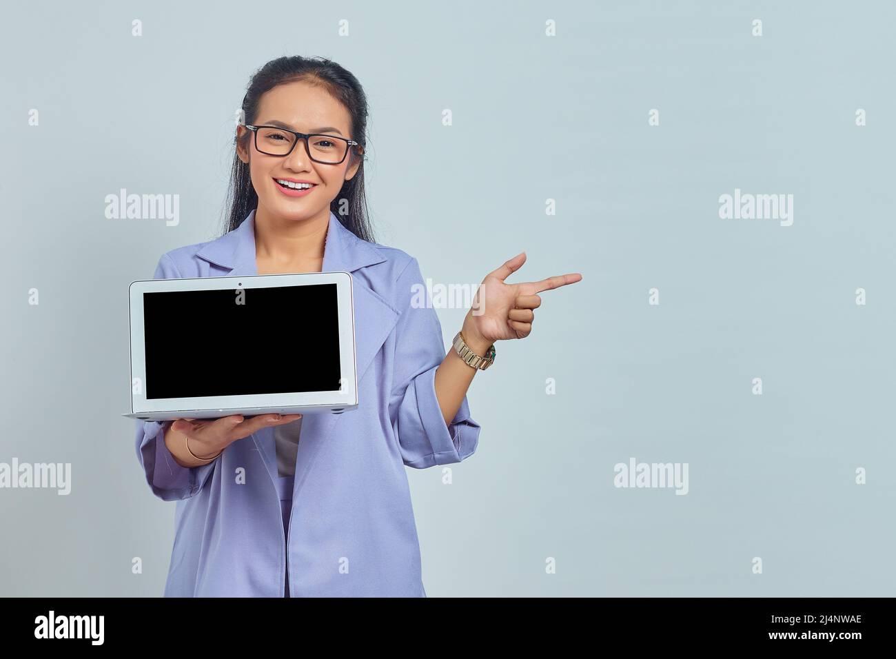Portrait of smiling young Asian woman showing blank laptop screen and ...