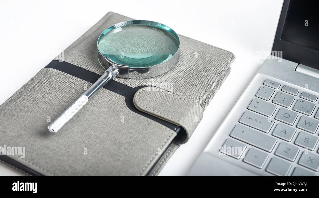 Magnifying glass at notebook with open laptop. Schedule, agenda ...