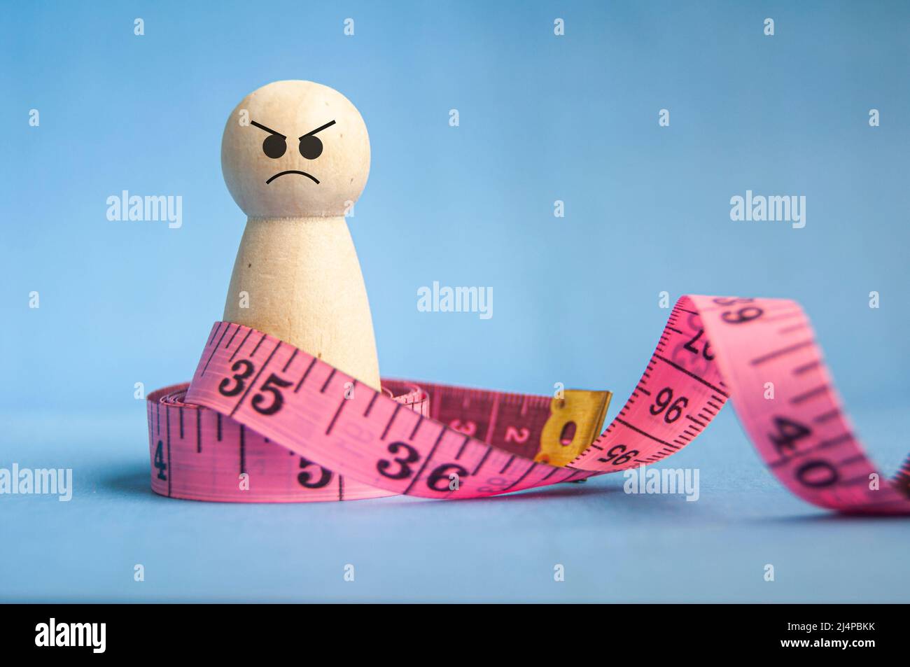Diet and weight loss concept. Wooden doll with angry face wrapped with ...