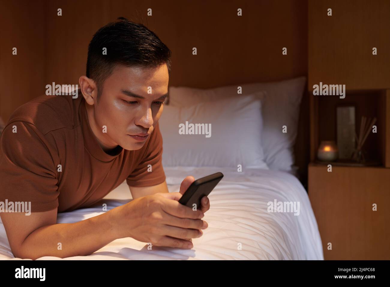 Serious young man resting on bed and answering text messages from his ...