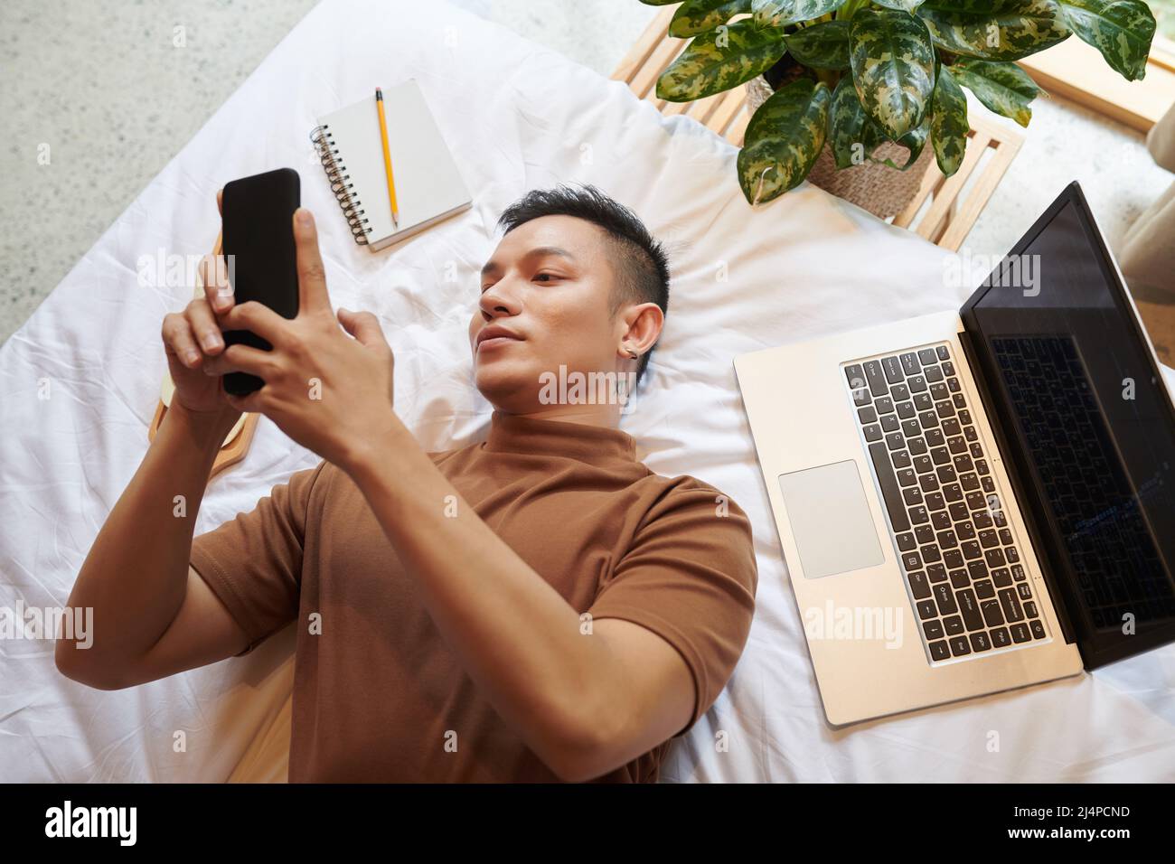 Yuong man lying on bed, texting friends or checking social media on ...