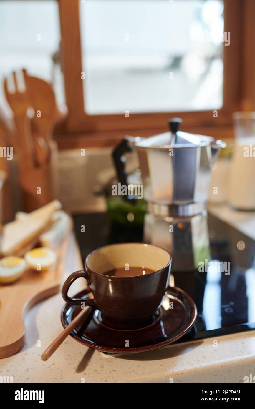 Cup of coffee on kitchen counter next to stove with moka pot on it ...
