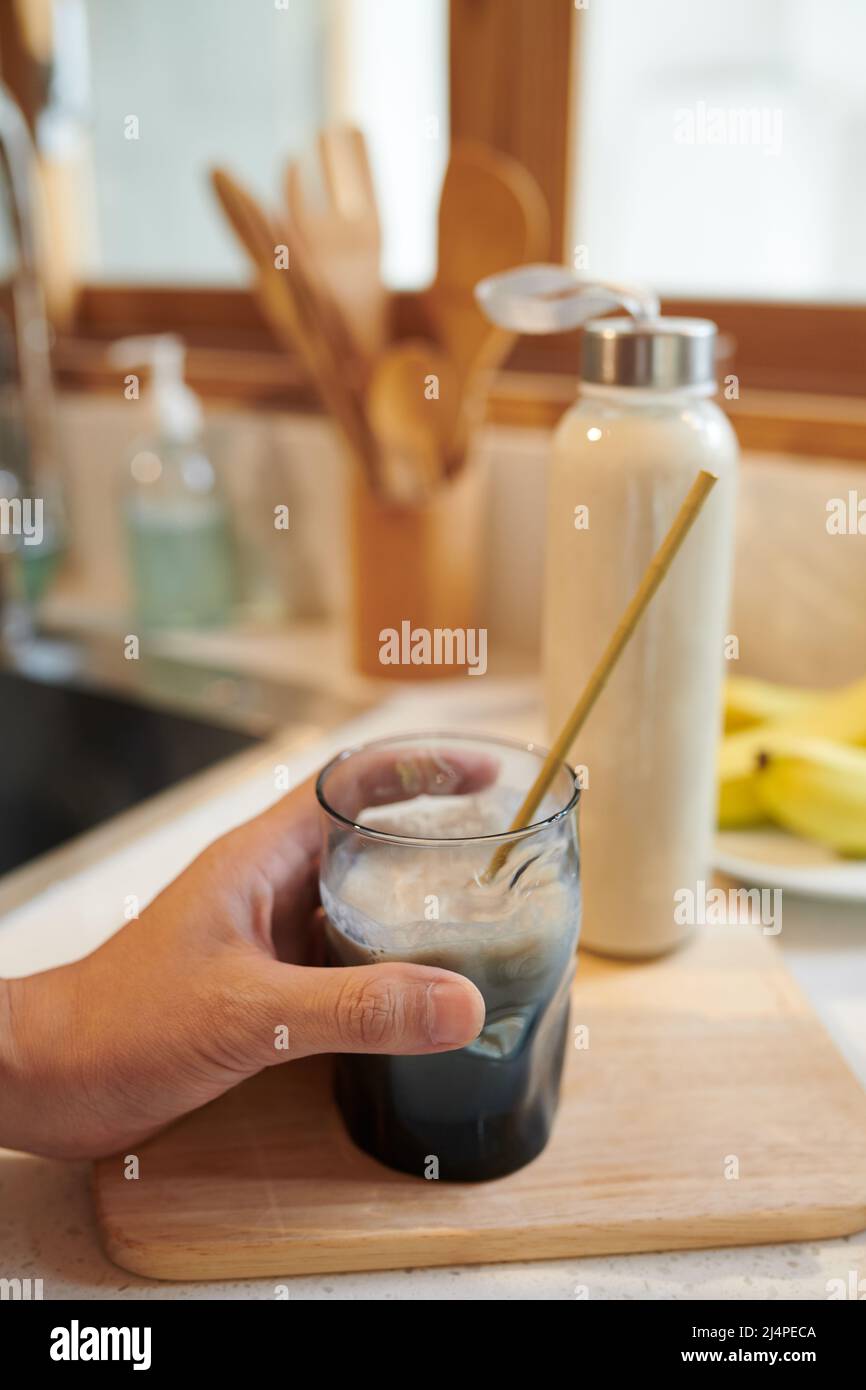 Hand of man holding glass of protein shake with reusable bamboo straw ...