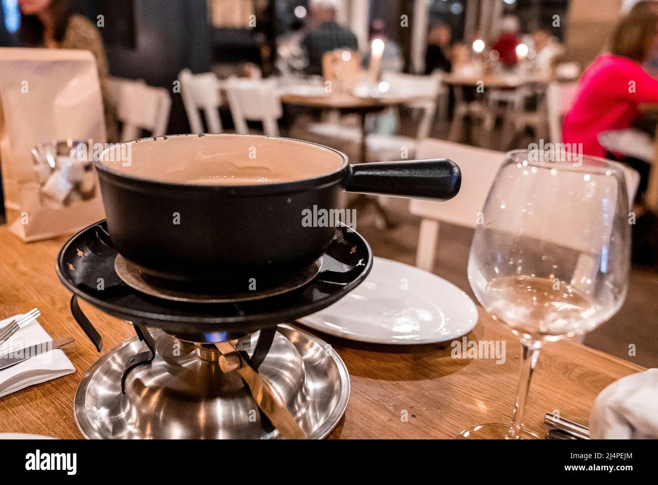 Heated pot of swiss cheese fondue alongside wineglass on dining table ...