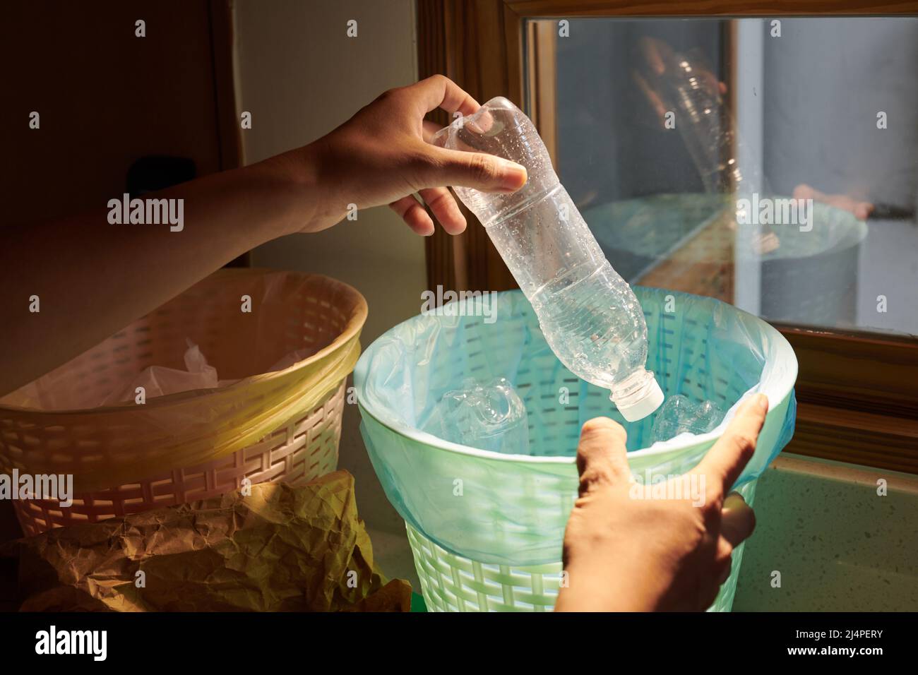Young man sorting waste at home and putting plastic bottle in separate ...