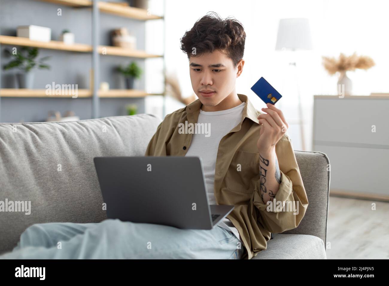 Focused asian guy showing using credit card at home Stock Photo - Alamy