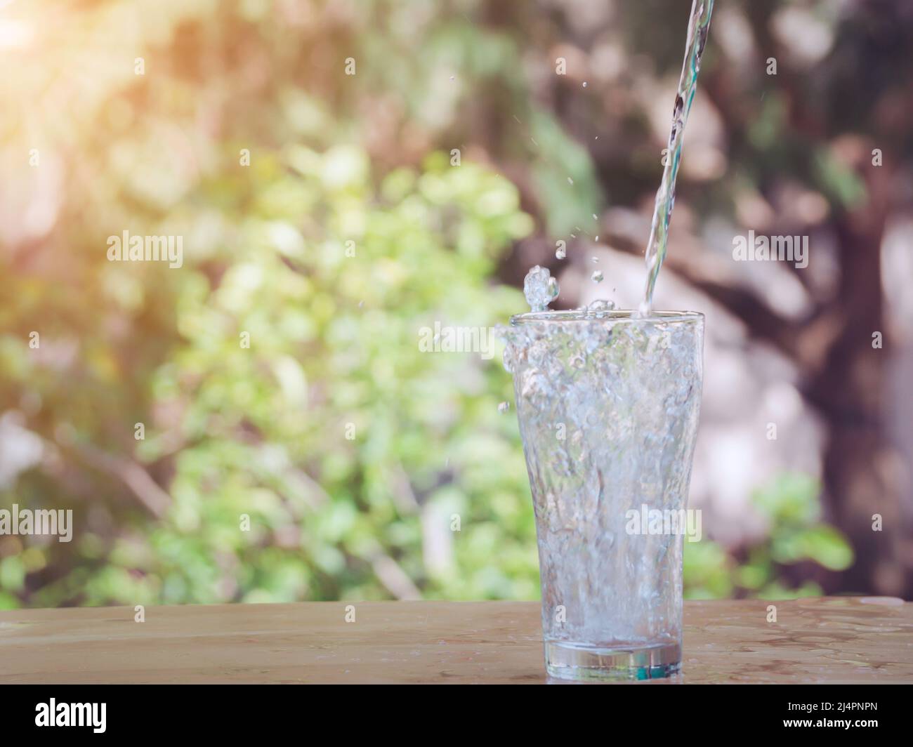 The pure water from jug into glass on wooden table on nature background ...