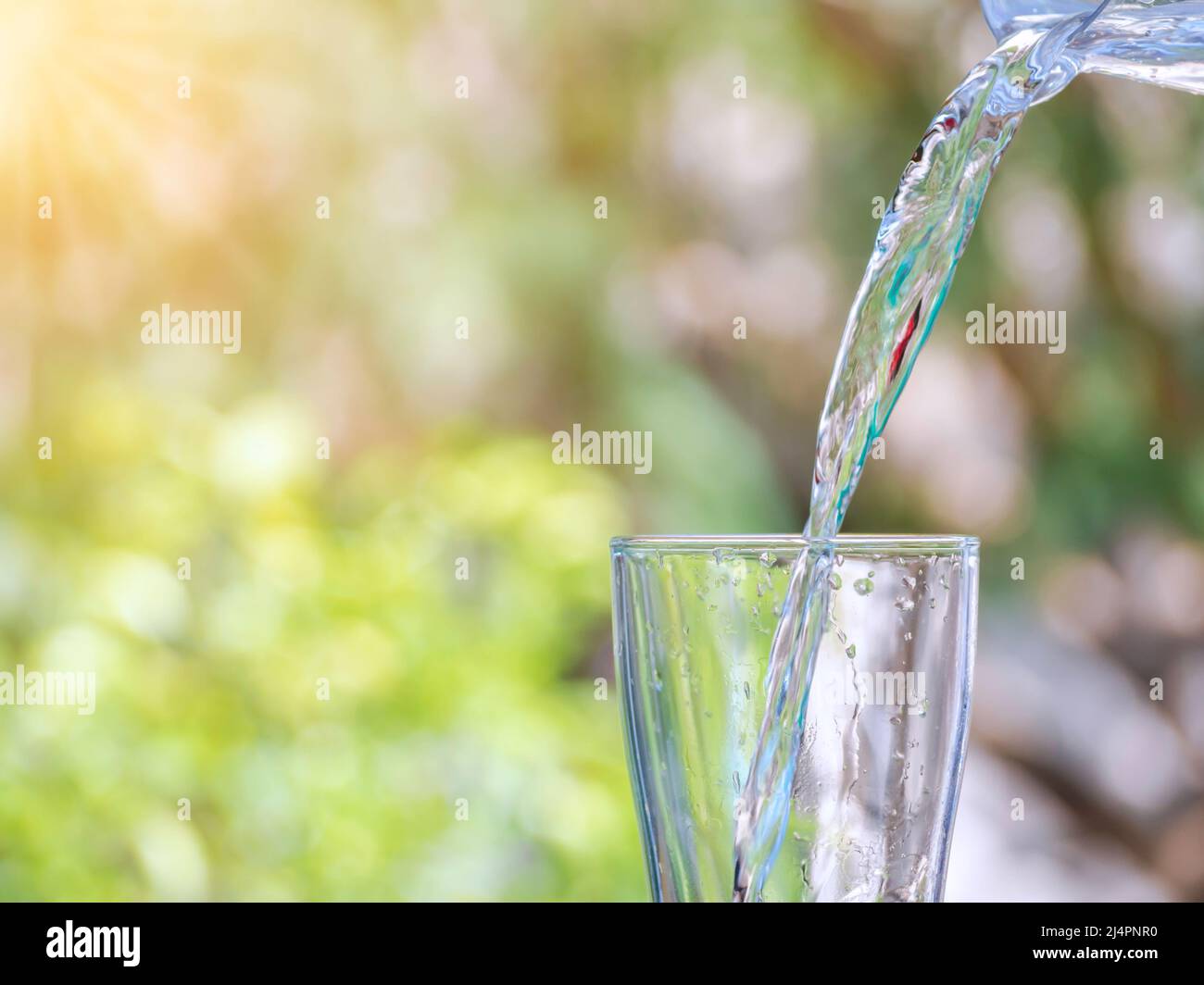 The pure water from jug into glass on wooden table on nature background ...