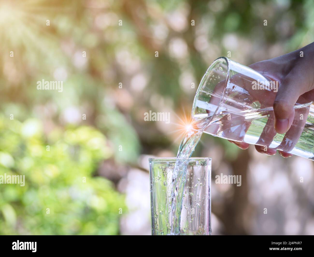 The pure water from jug into glass on wooden table on nature background ...