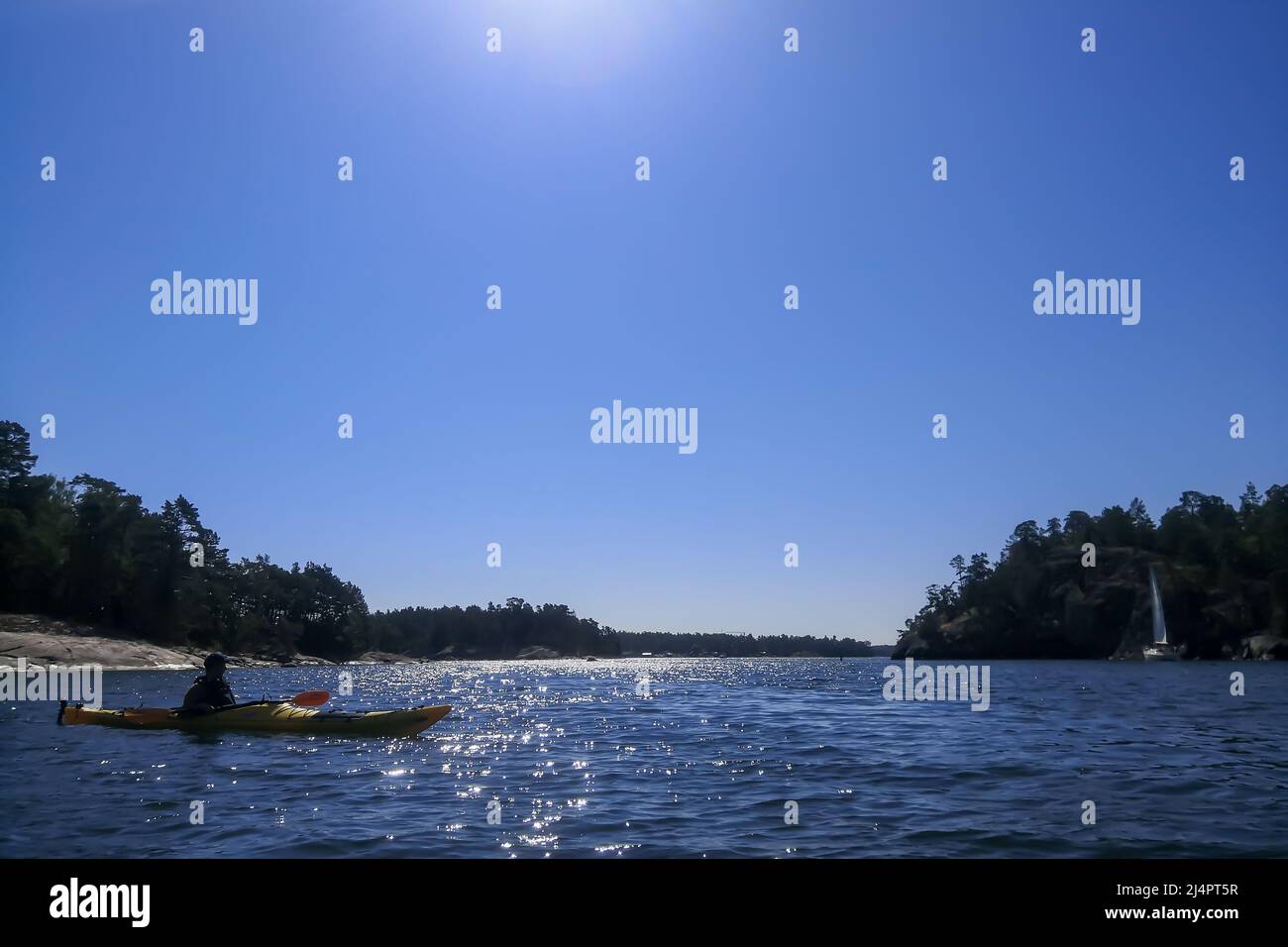 Young man is kayaking in a blue water Swedish archipelago on a summer ...