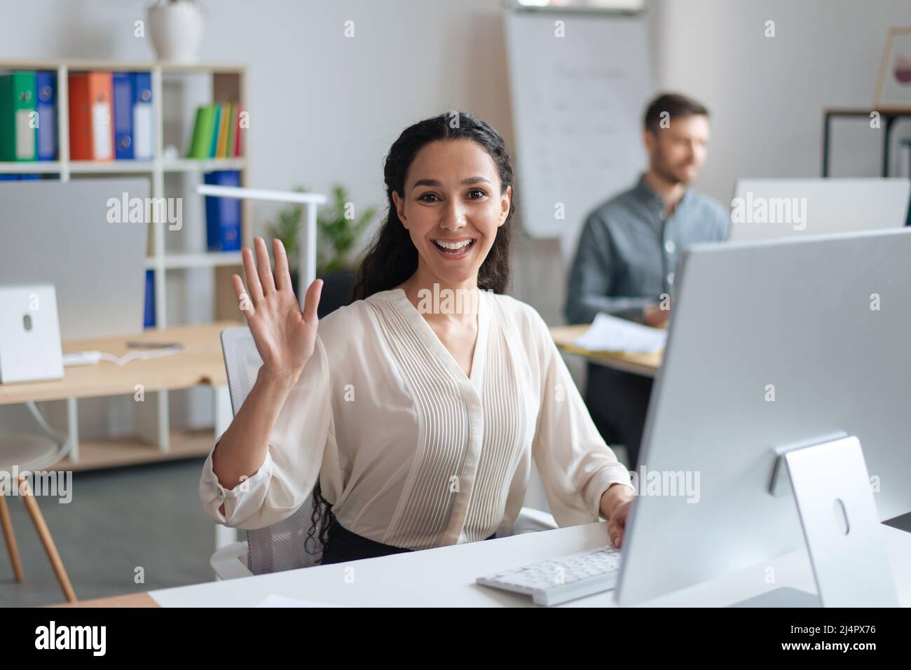 Happy young woman working on modern computer, smiling and waving at ...