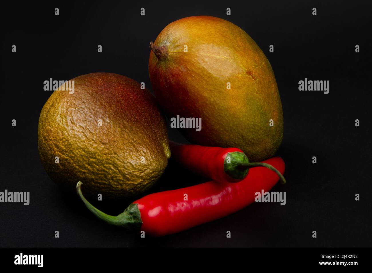 Wrinkled mango and smooth mango with red hot chili pepers on black ...