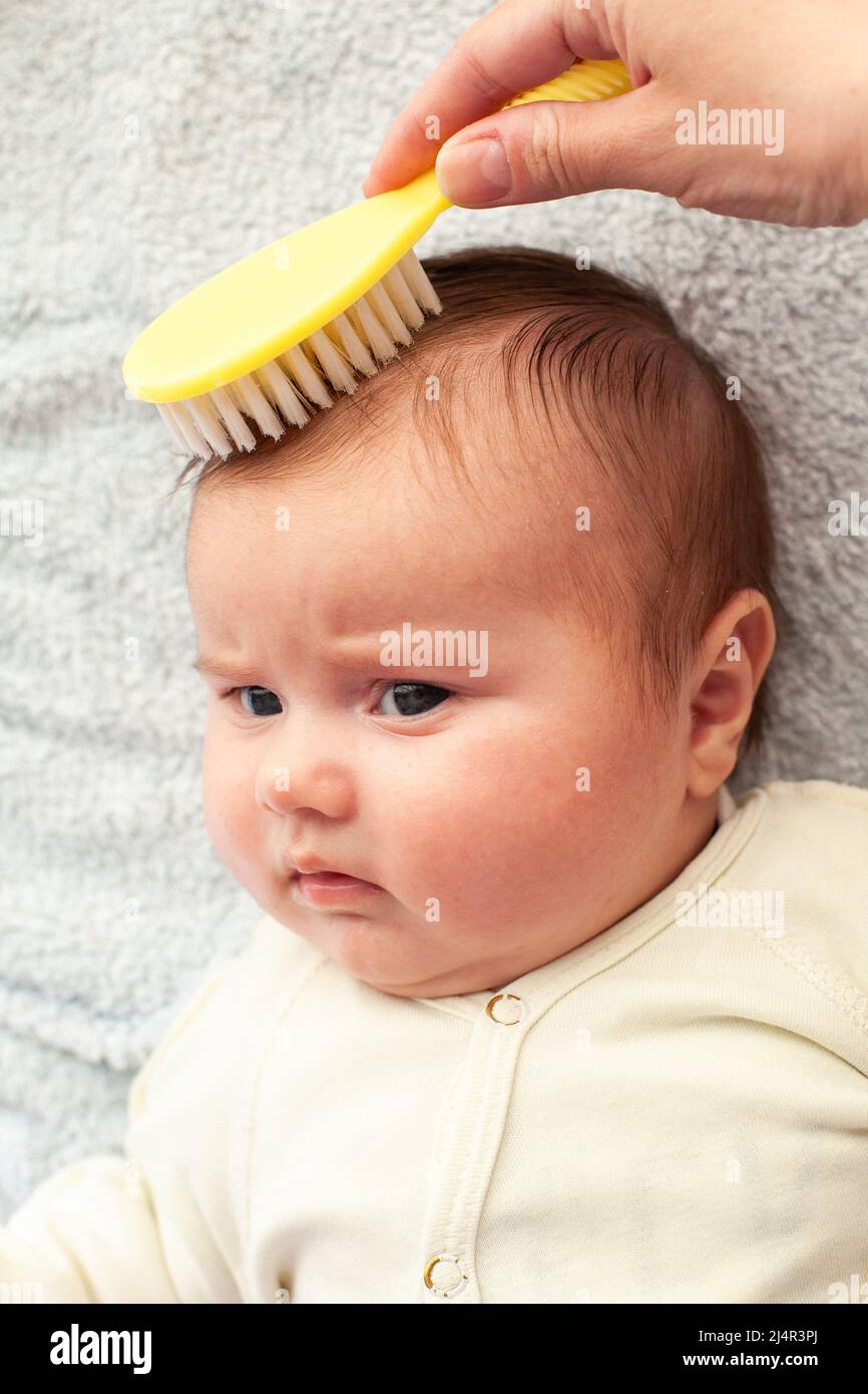 Mom combs a newborn baby with a special hair brush. Maternity concept ...