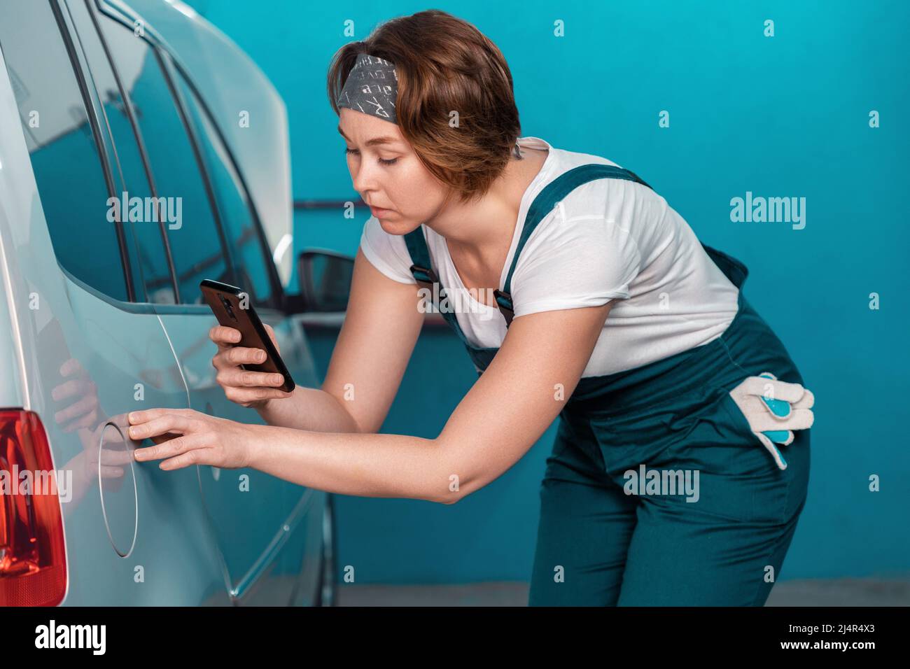 Female mechanic in overall check with device scratches of car. The ...