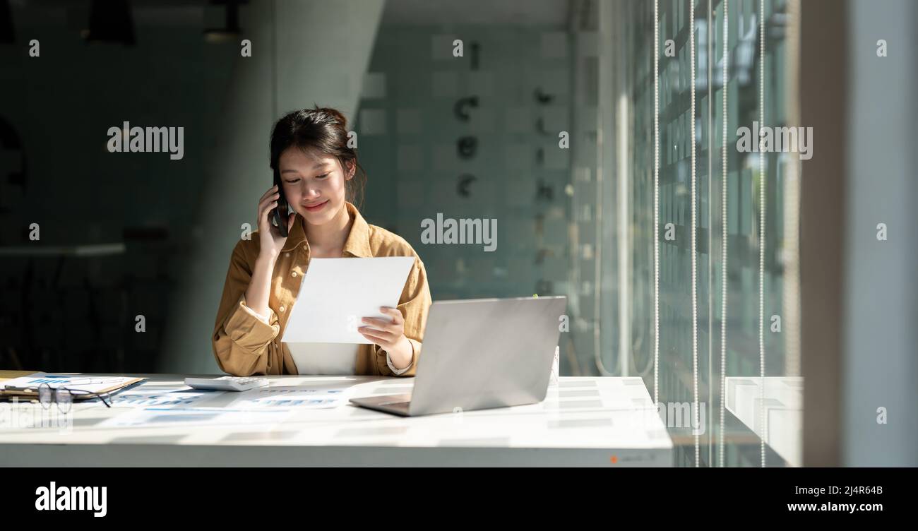 Young asian accountant calling marketing consultants and using laptop ...