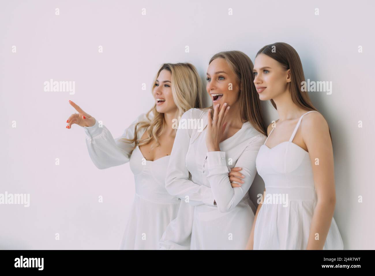 Pleased three women smiling pointed side over white wall Stock Photo ...